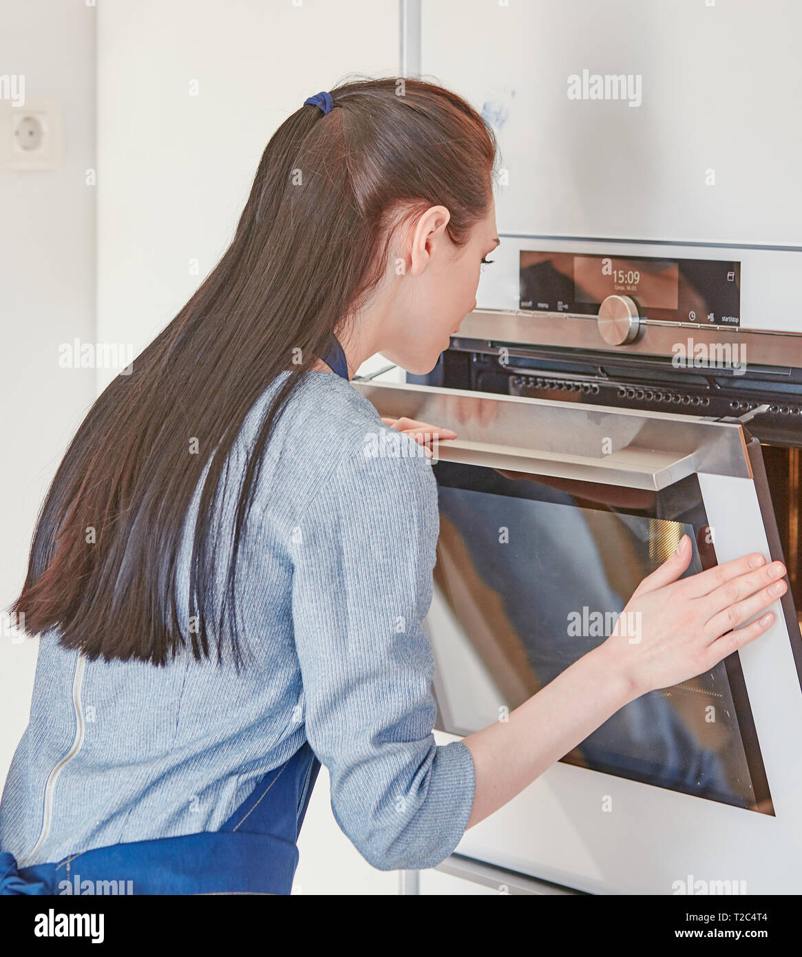 Beautiful woman in the kitchen, waiting with the front of the oven ...