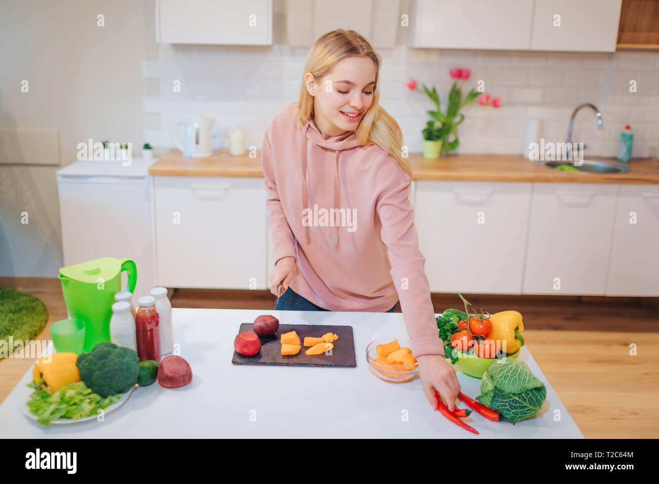 Vegan beautiful blonde woman cooking raw vegetables in the kitchen. Raw ...