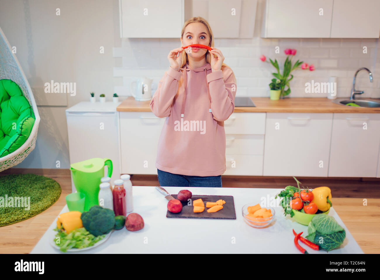 Vegan beautiful blonde woman has fun with chili peper while cooking raw ...