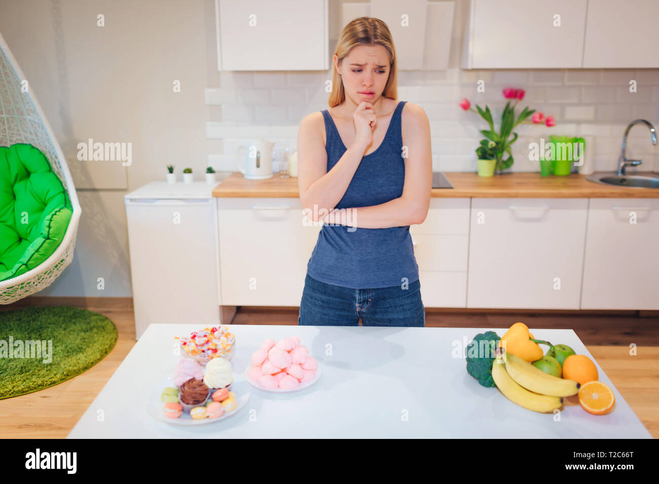Young sad woman in blue T-shirt choosing between healthy and unhealthy ...