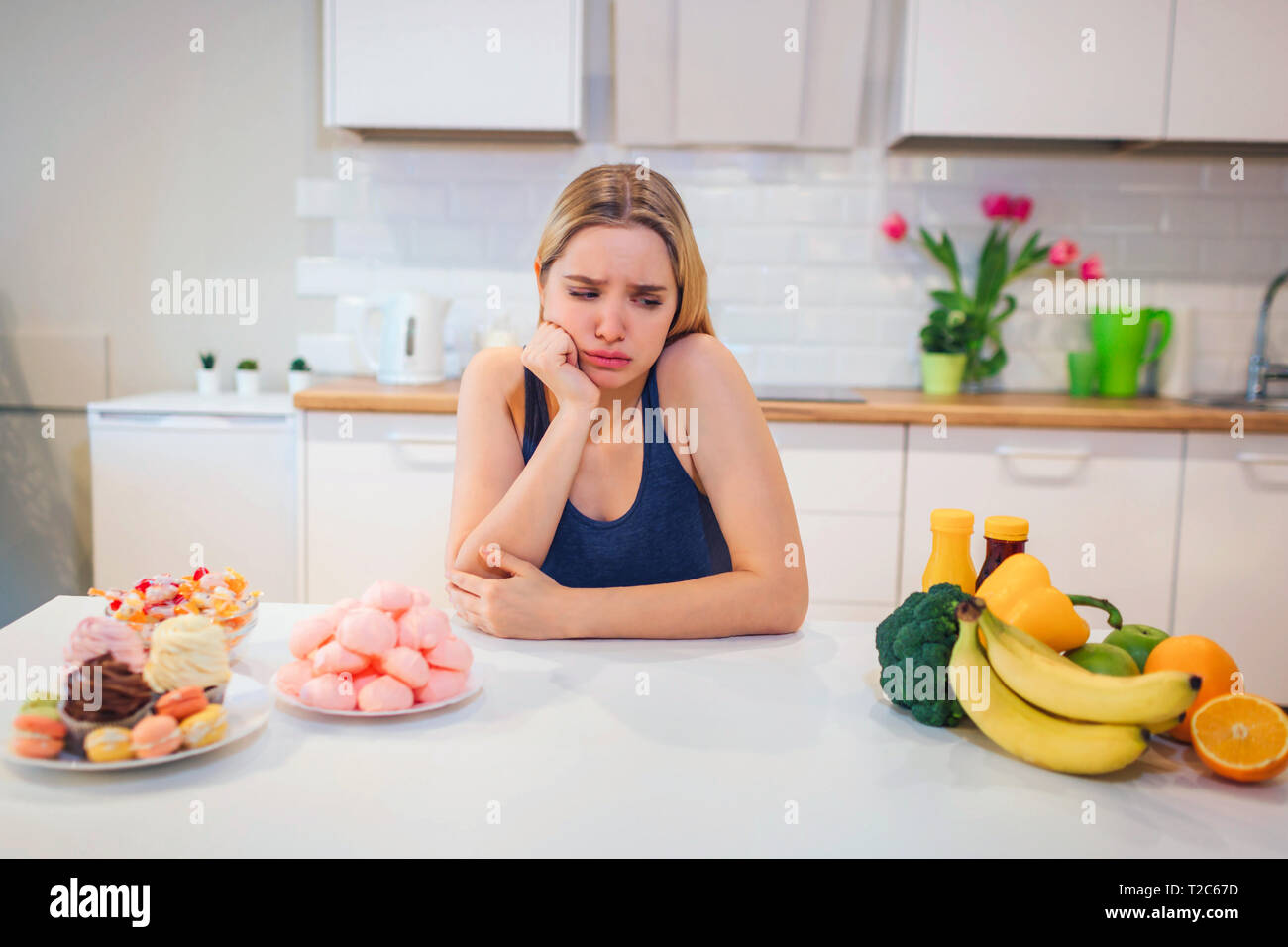 Diet struggle. Young sad woman in blue T-shirt choosing between fresh ...
