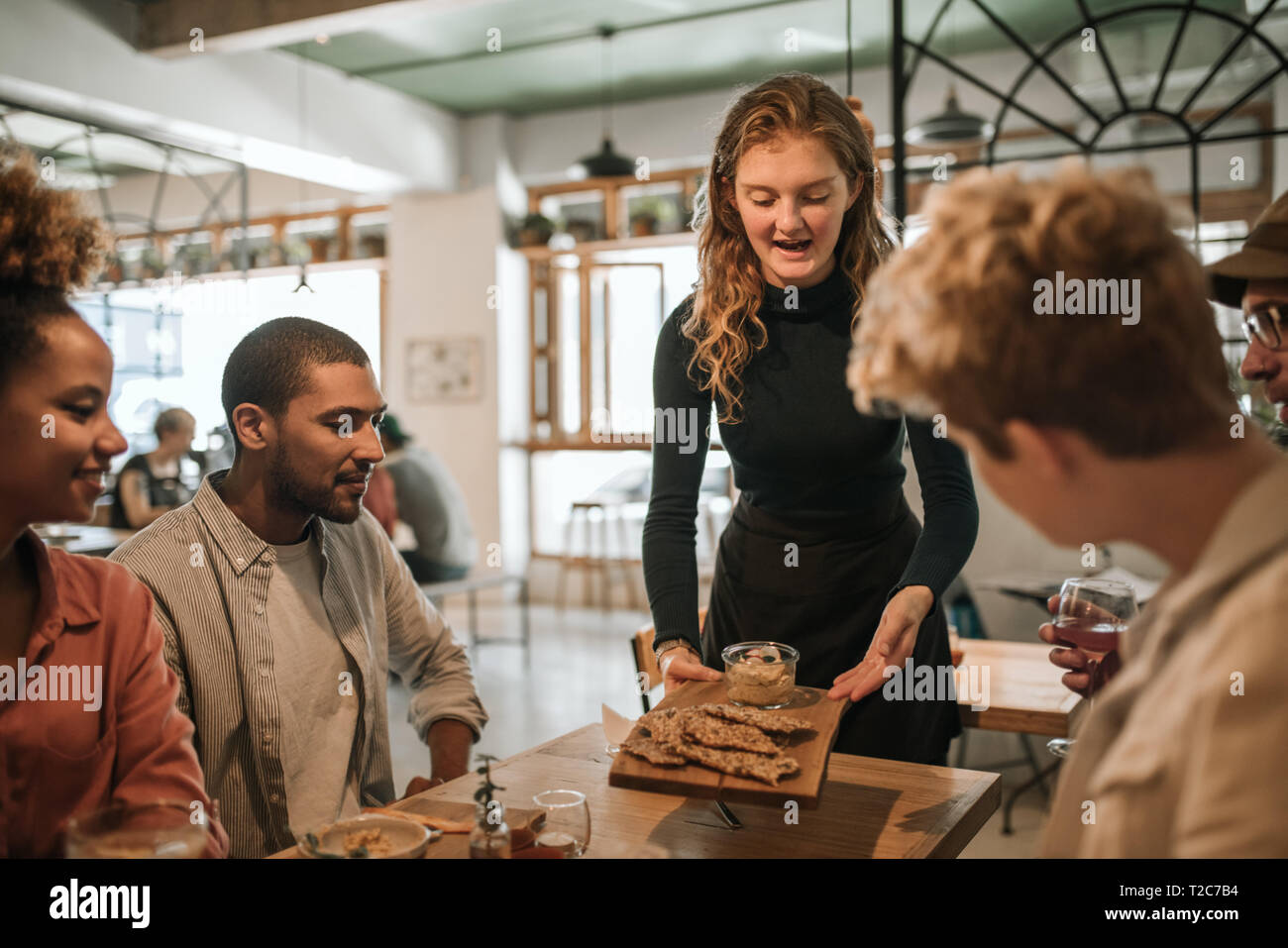 Smiling waitress bringing a food order to a group of young friends ...