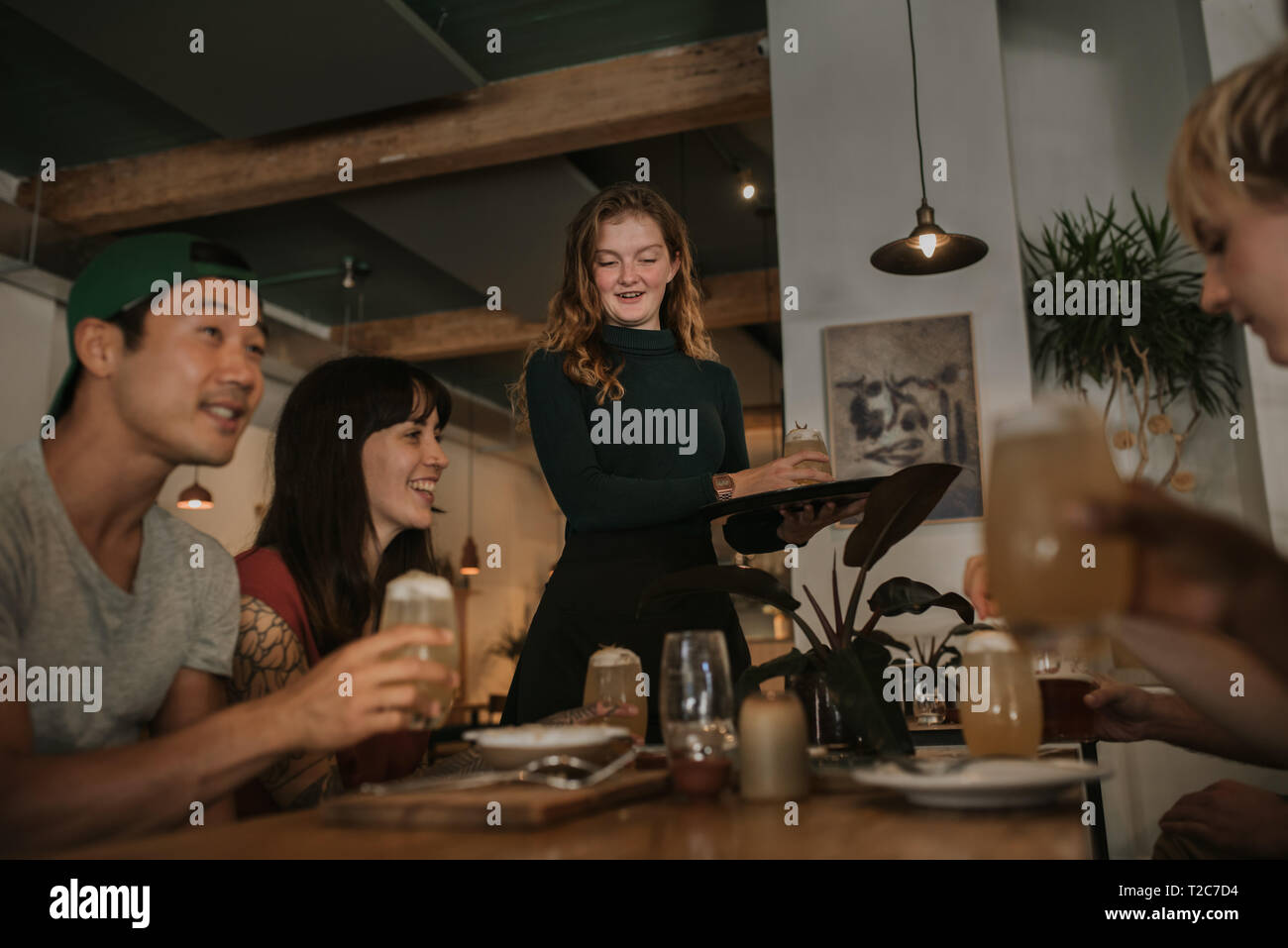Smiling waitress bringing a drinks order to a group of young friends ...