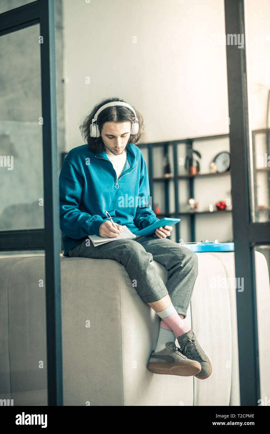 Chilling concentrated guy sitting on back of the couch with headphones ...