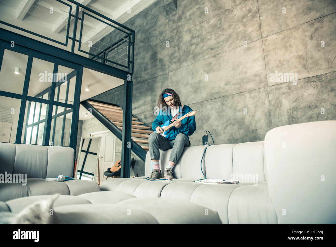 Long-hired talented guy sitting on the couch while training his skills ...