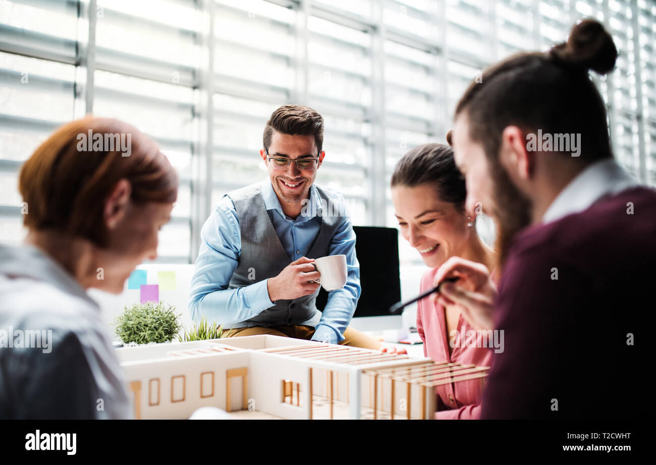 A group of young architects with model of a house working in office ...