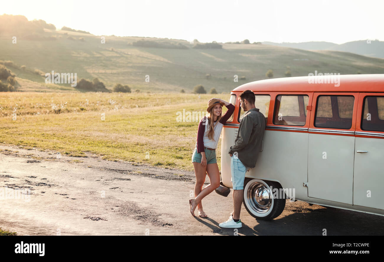 A young couple on a roadtrip through countryside, standing by retro ...