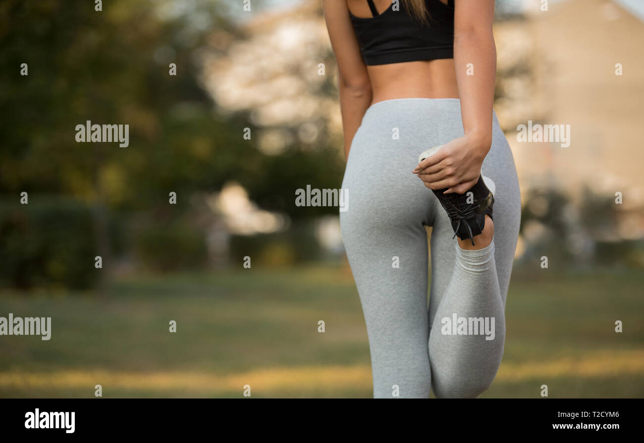 Young fitness woman runner stretching legs before run in park, back view, empty space Stock ...