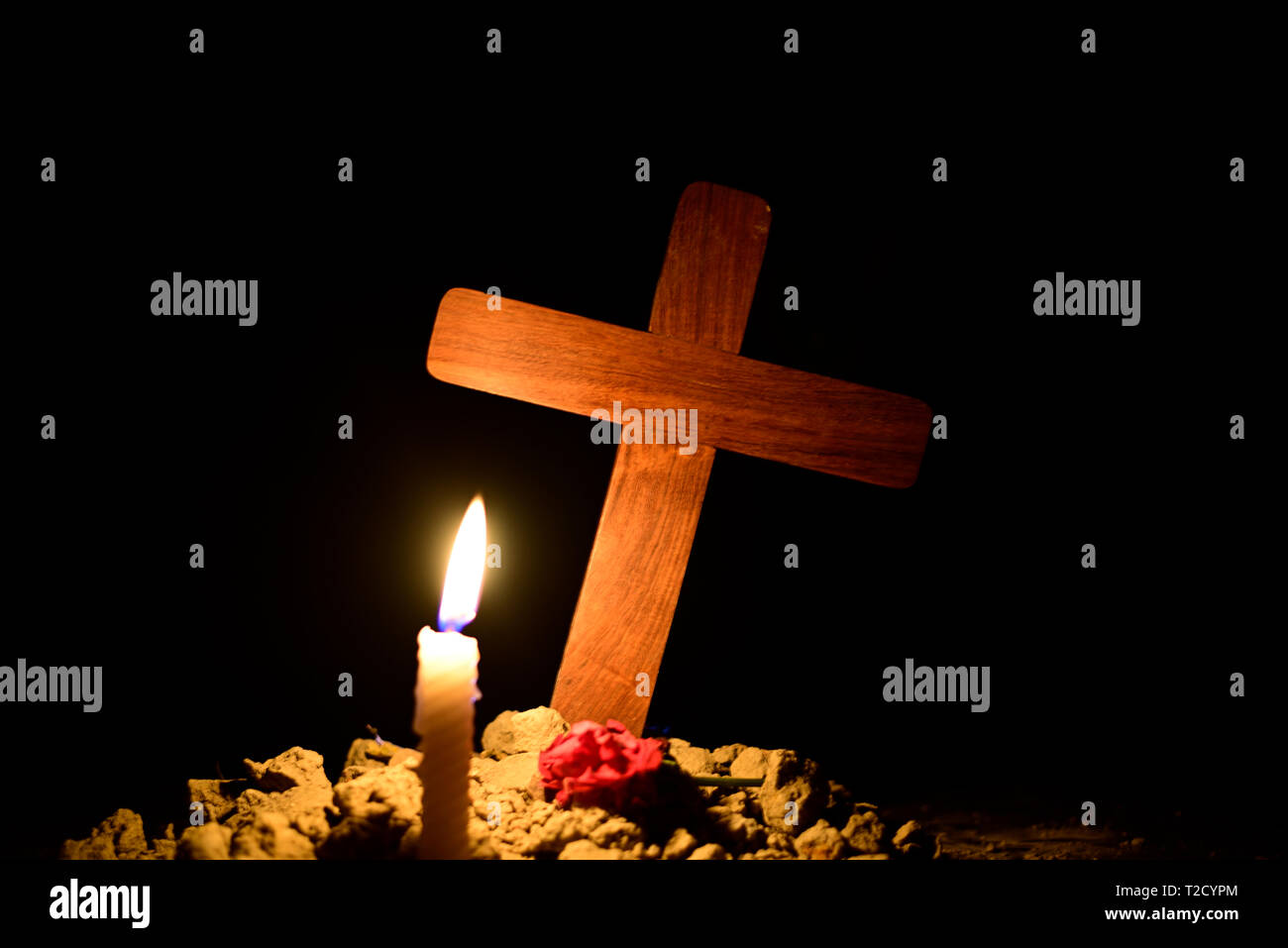 Burning candle under Jesus cross in a cemetery against black background ...