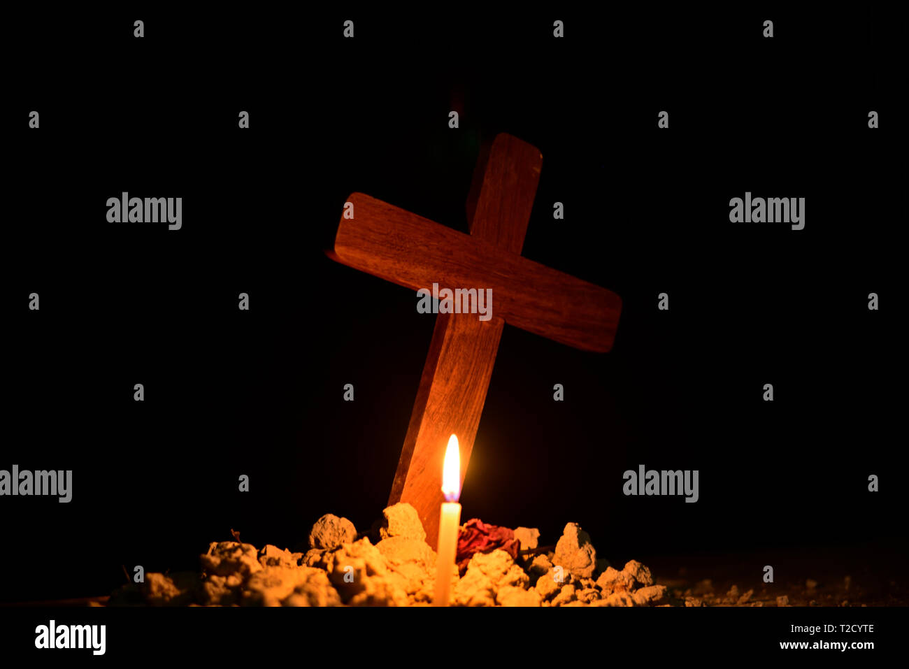 Burning candle under Jesus cross in a cemetery against black background ...