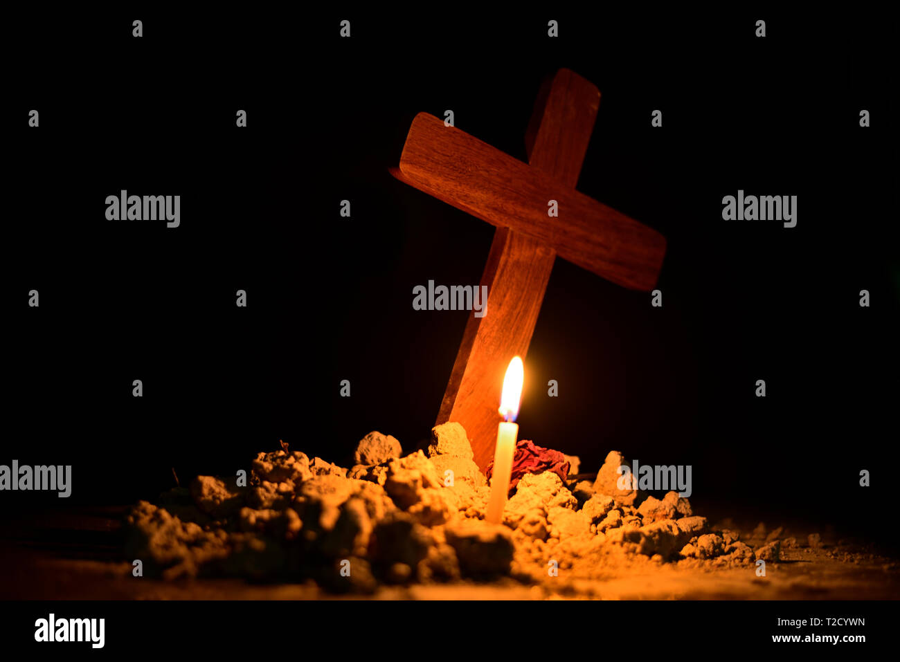 Burning candle under Jesus cross in a cemetery against black background ...