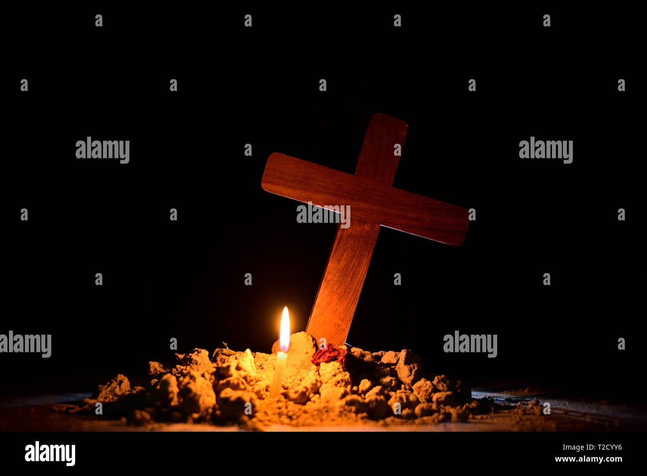 Burning candle under Jesus cross in a cemetery against black background ...