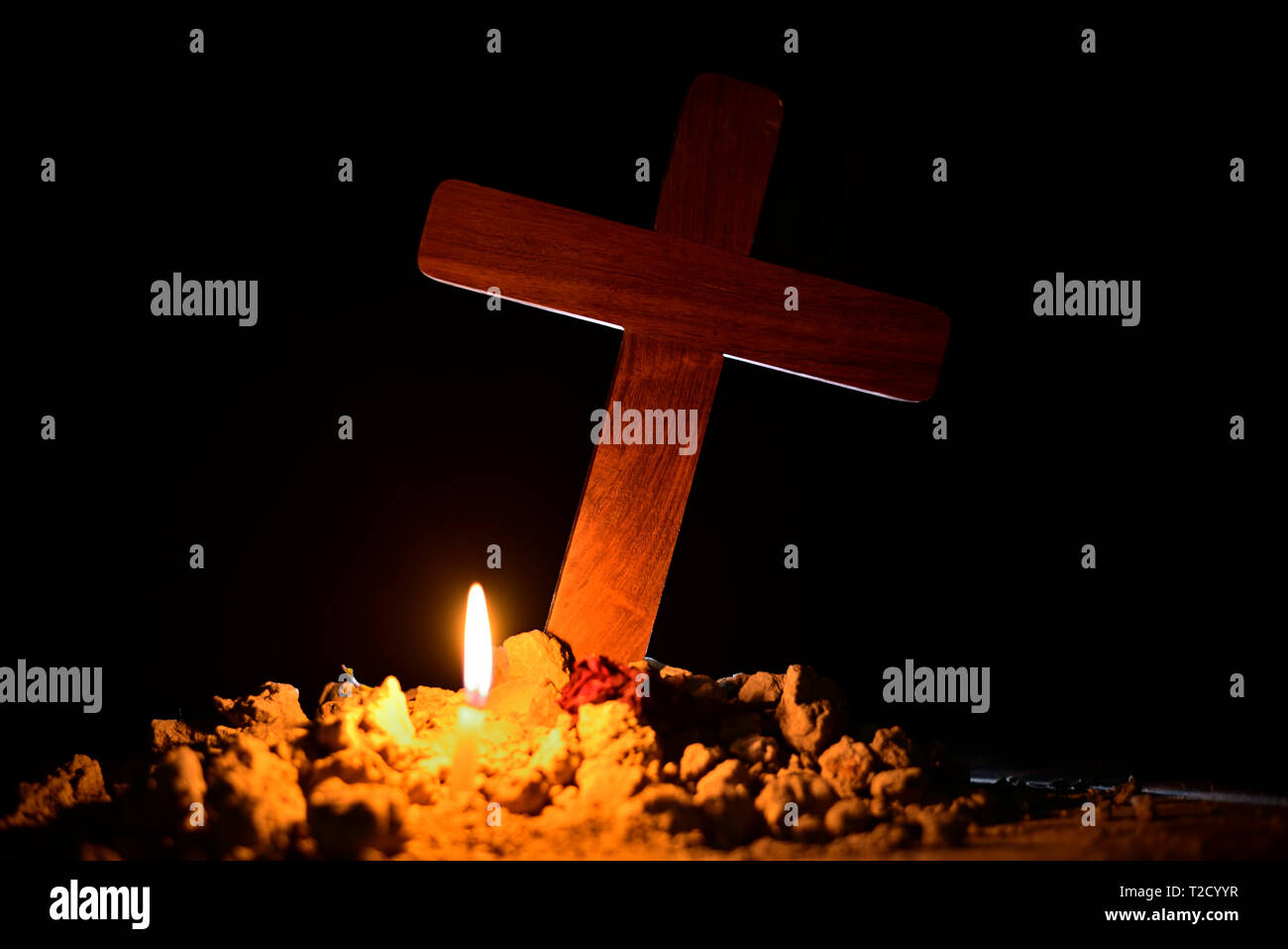 Burning candle under Jesus cross in a cemetery against black background ...