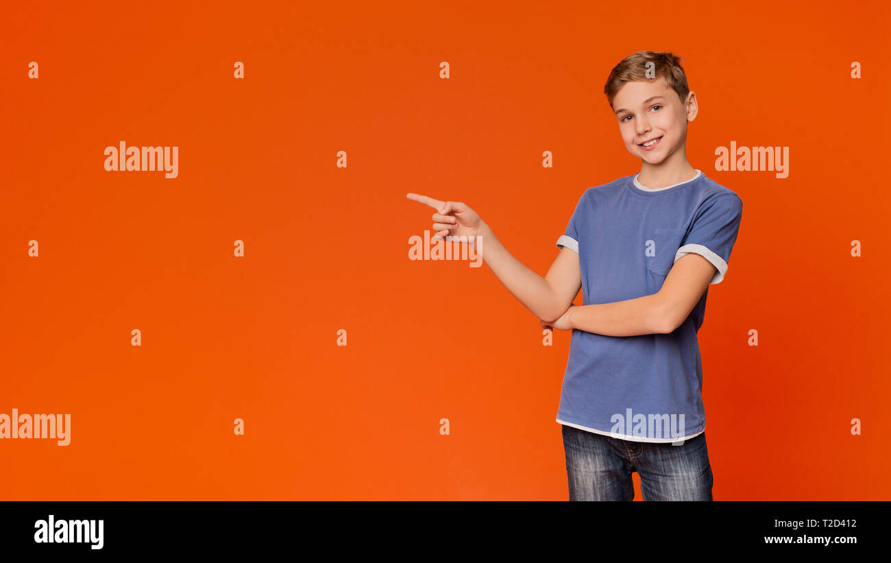 Cool confident school boy pointing away at free space on orange studio ...