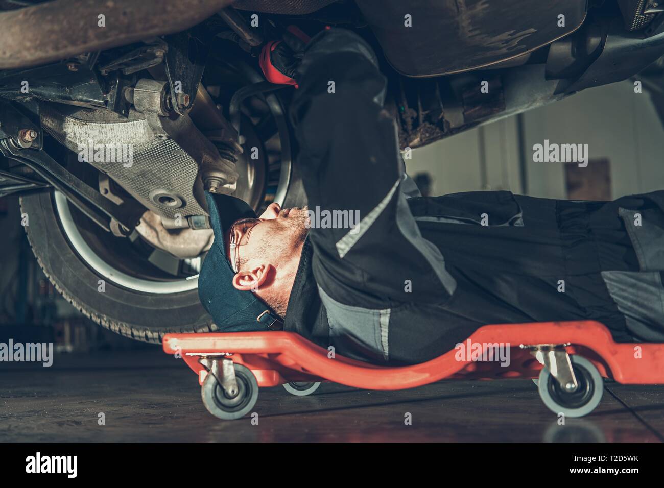 Caucasian Car Mechanic on a Creeper Performing Vehicle Repair Inside ...