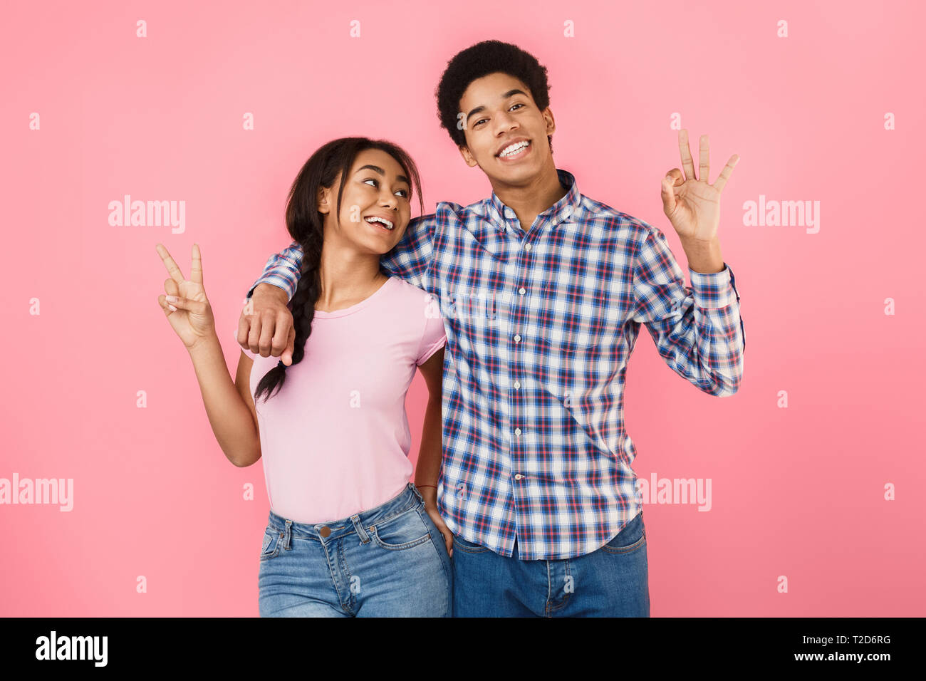 Happy students showing ok and peace gesture, posing over pink ...