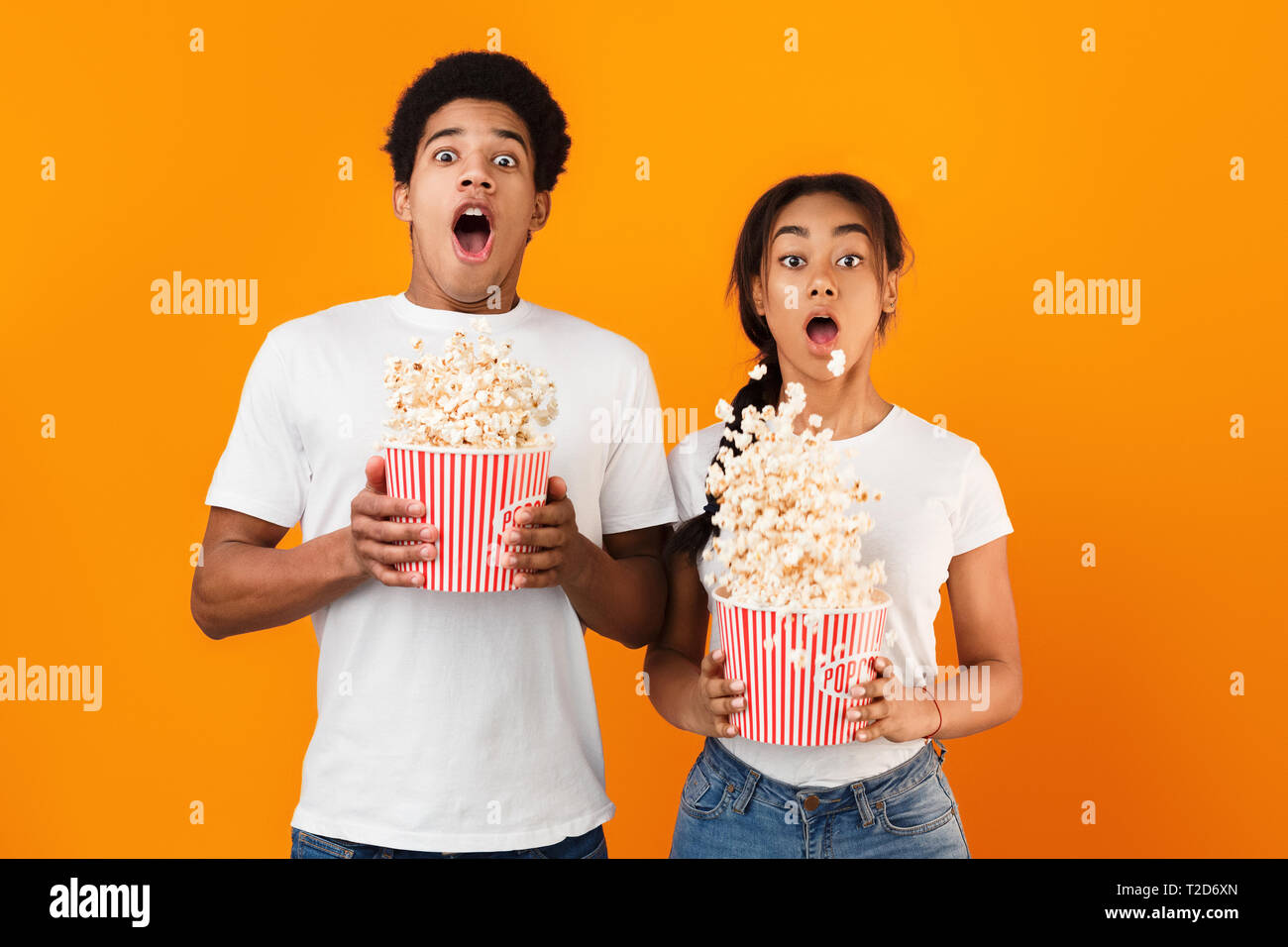 Horror film. Frightened couple throwing popcorn over orange background ...
