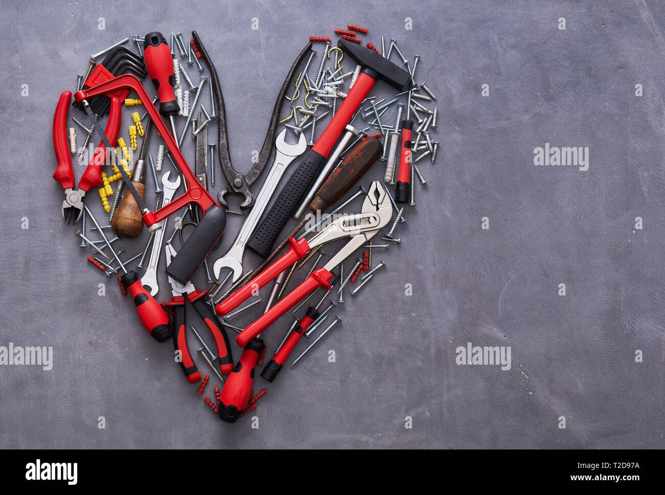 Heart shaped still life of red hand tools and screws on grey with ...