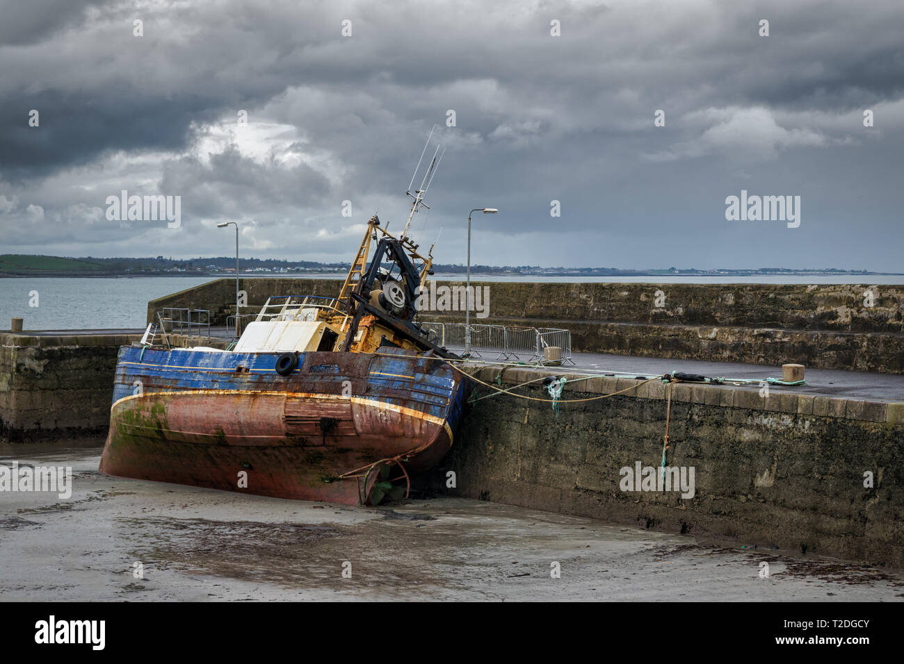 This is an old fishing boat tide up to a pier at low tide. It is ...