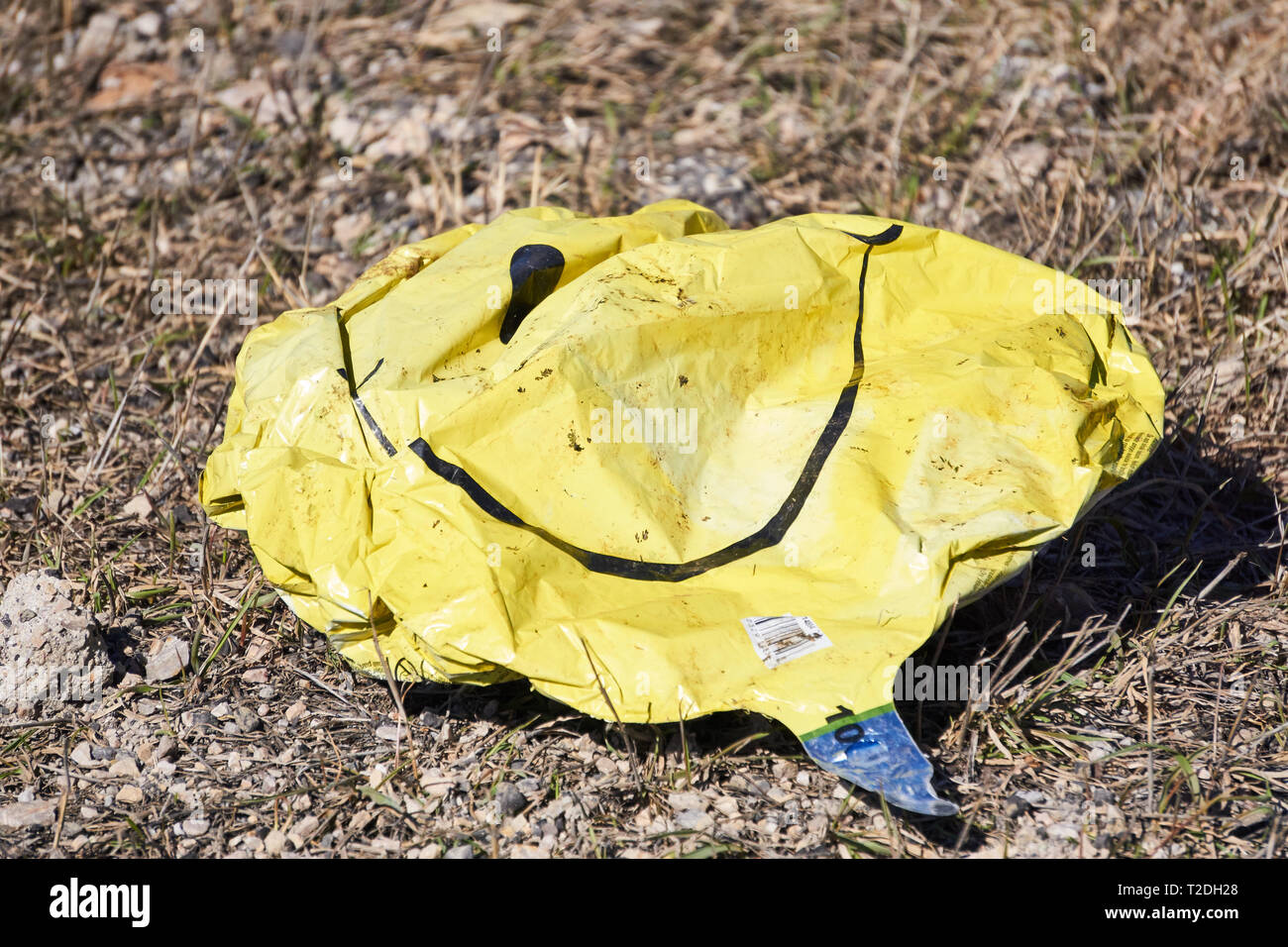Empty, deflated mylar smiley face yellow balloon on the ground outside ...
