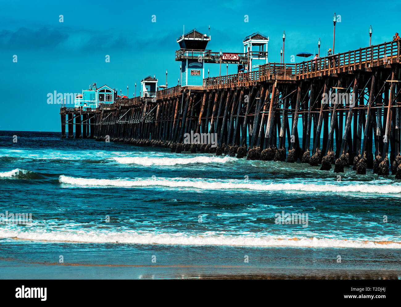 Wooden pier with buildings and people under blue skies with blue ocean ...