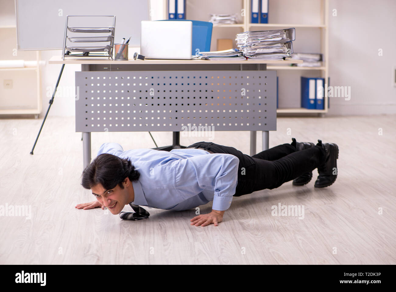 Young handsome male employee doing exercises in the office Stock Photo ...