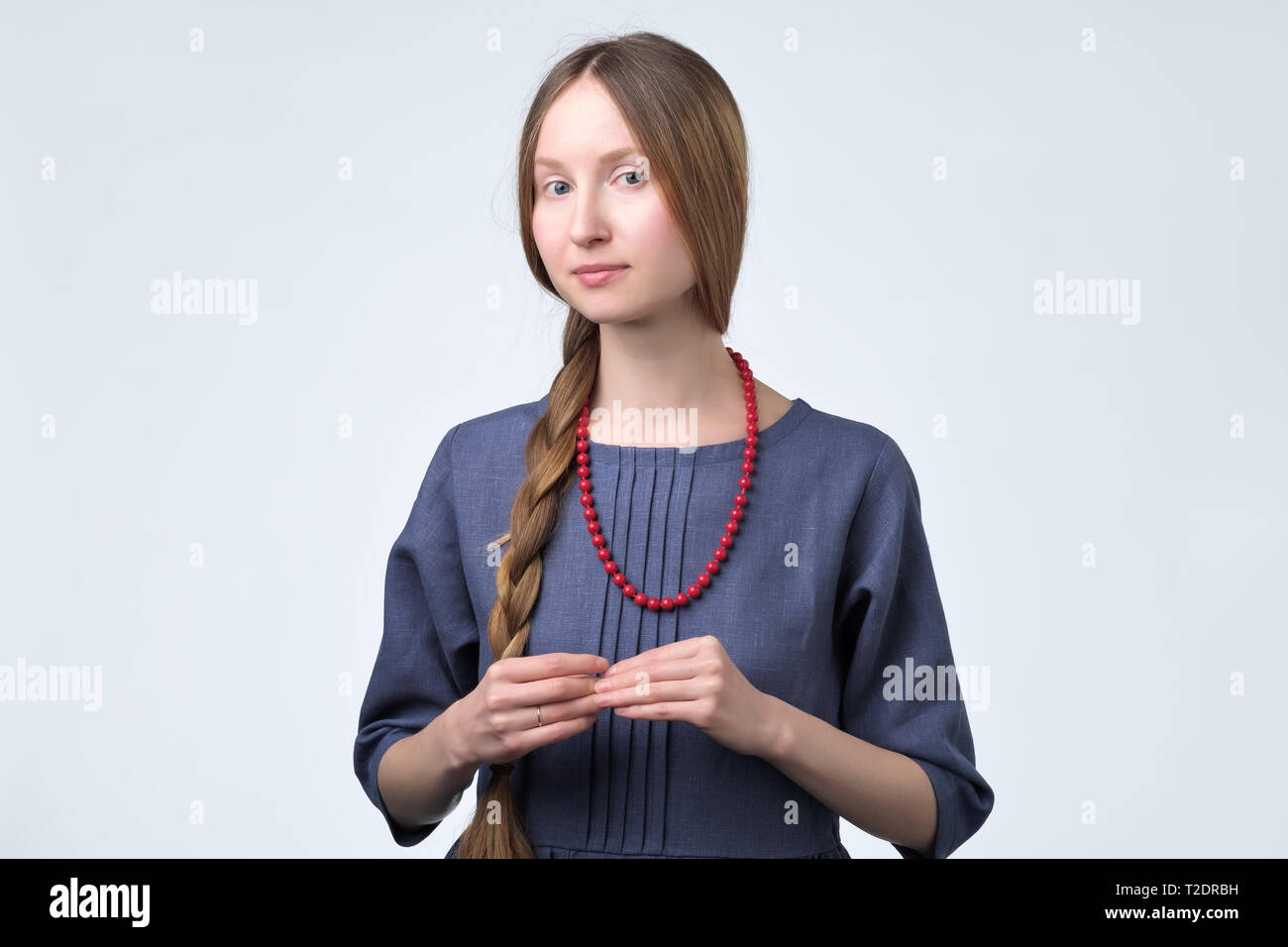 Lack of confidence. Shy young woman in blue dress with red beads feels ...