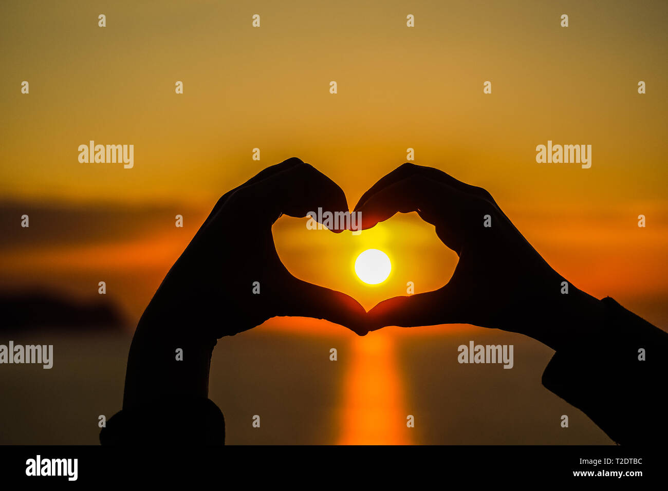 A heart made with hands with the sun inside it during sunset and ...