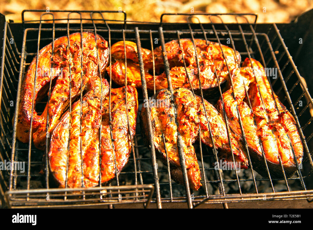 Grilling salmon steak with ginger marinade in wire rack over barbecue ...
