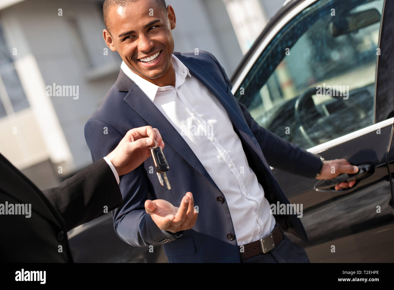Agent giving key to young mulatto businessman standing near car looking ...