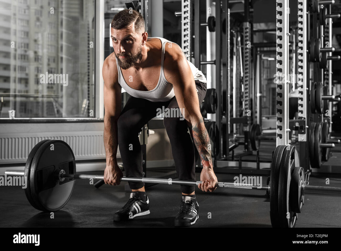 Bearded man bodybuilder exercising at gym bending down holding barbell ...