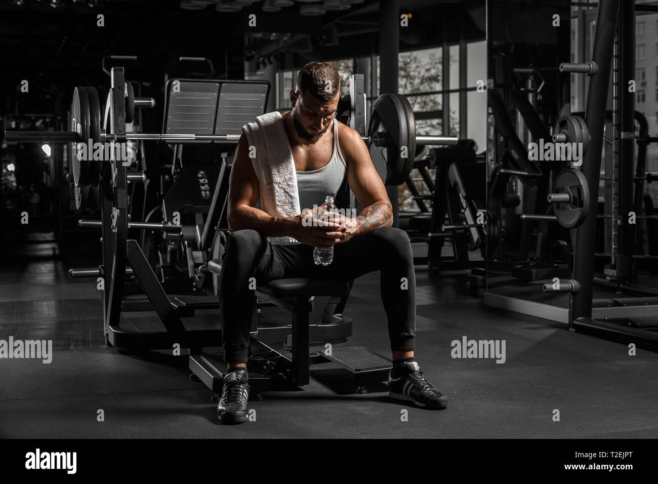 Bearded man bodybuilder sitting on bench at gym with towel holding ...