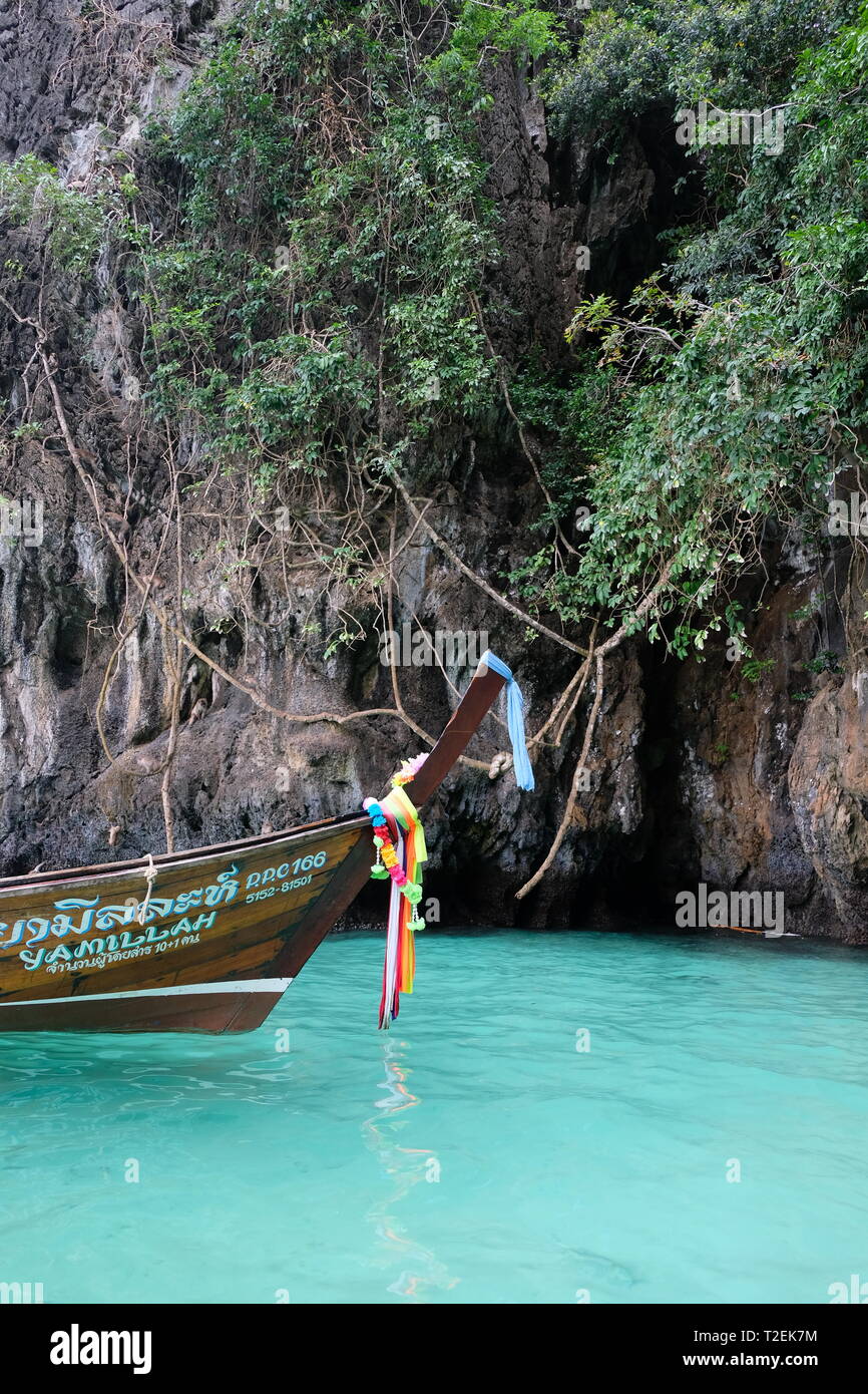 Long-tail boat floating on aqua sea next to large cliff Stock Photo - Alamy