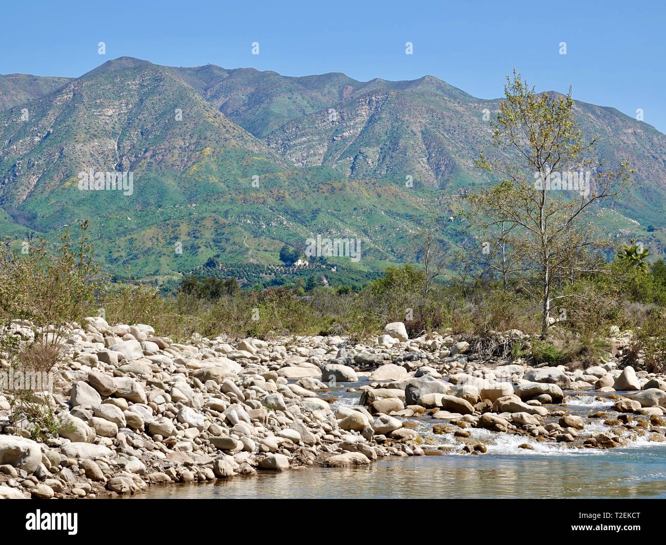 Large rocks, stones, line the edges of the Ventura River with Topatopa ...