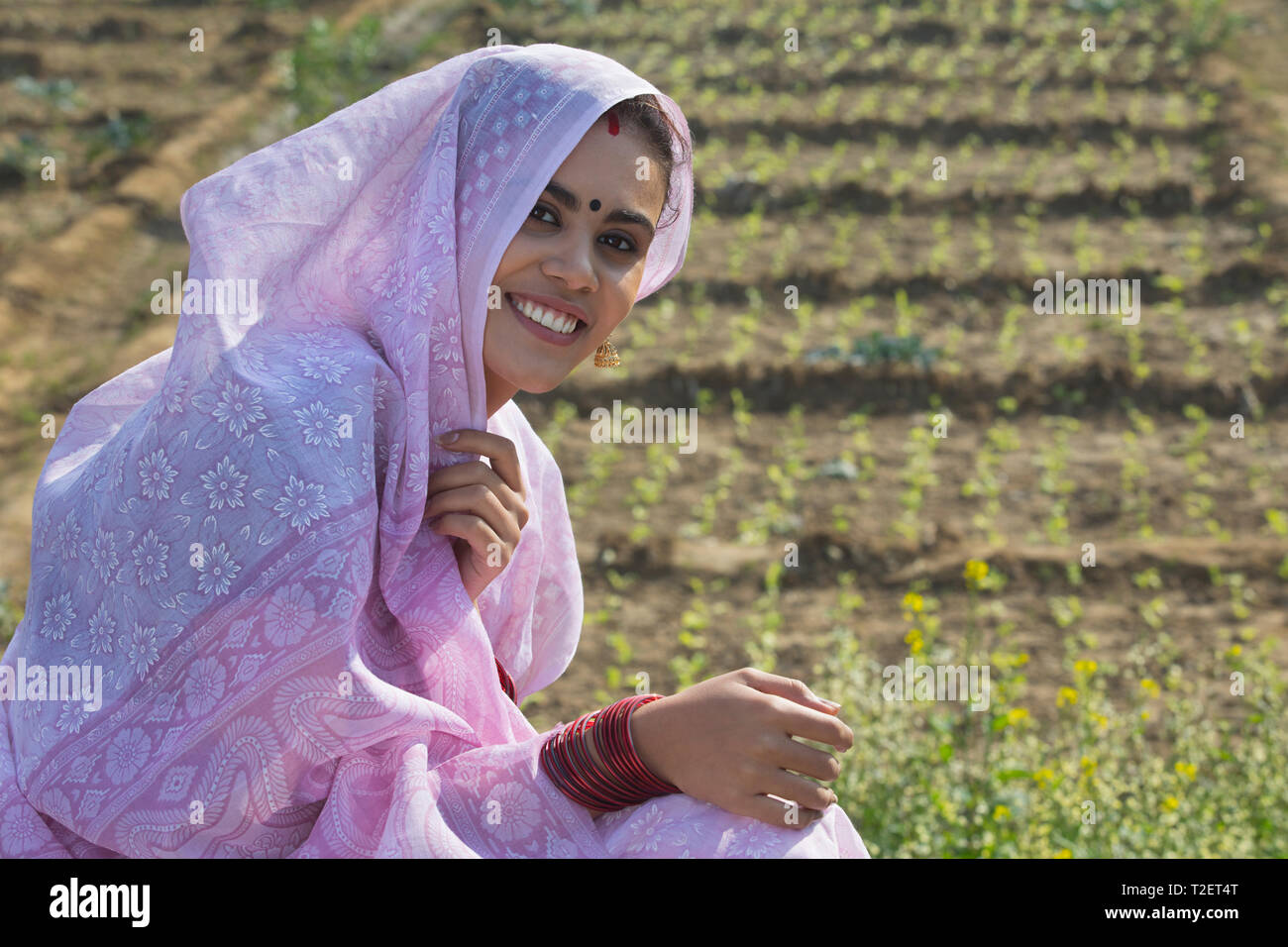 Closeup of a young smiling rural woman sitting in her agriculture field ...