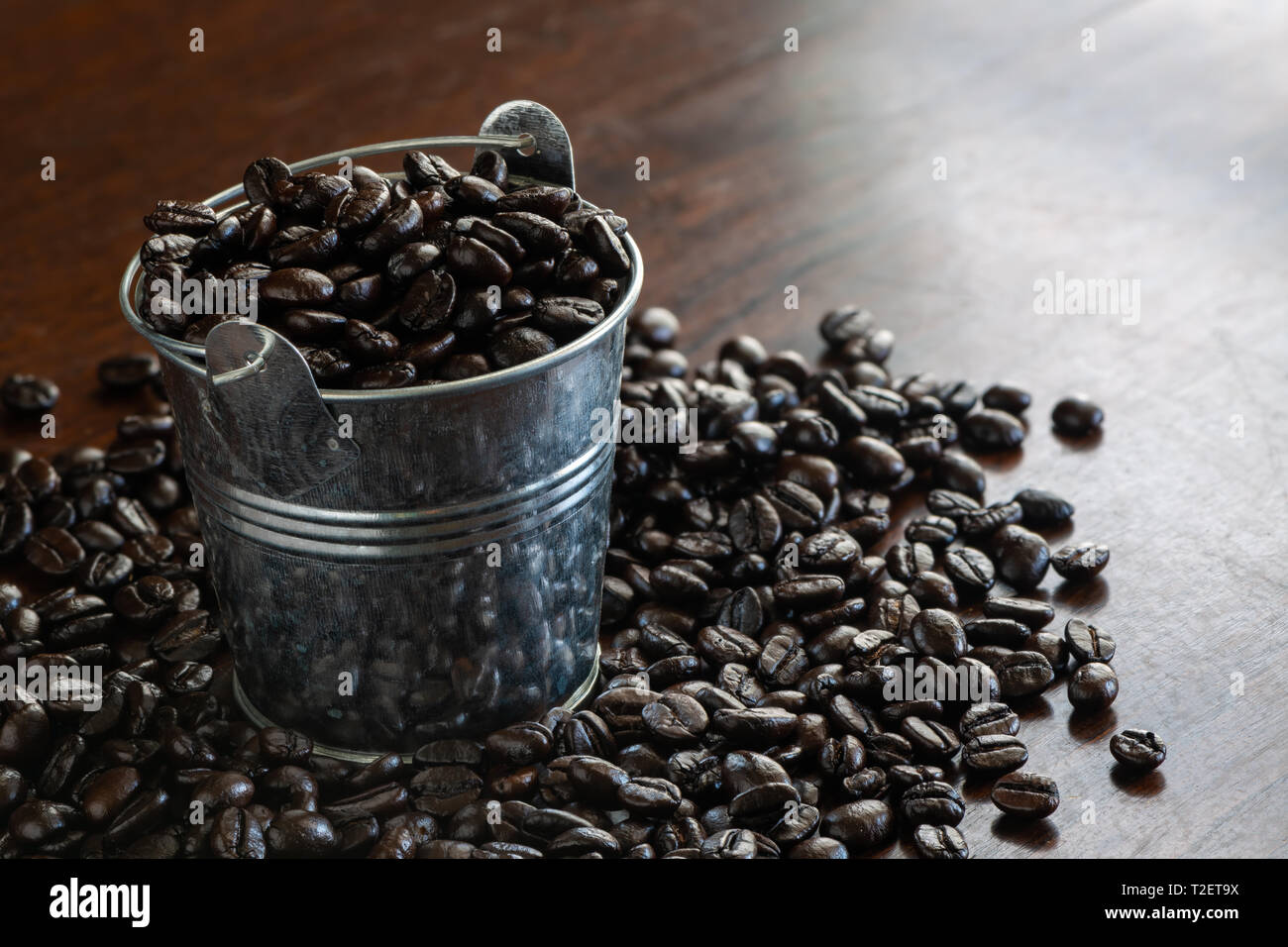 Coffee beans in a small bucket with some spreading on the wooden table ...