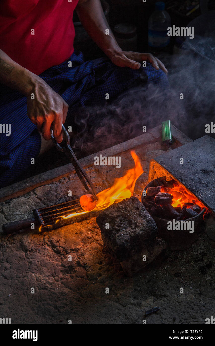 A Silversmith leans over a forge as he makes a silver ring, Shan state ...