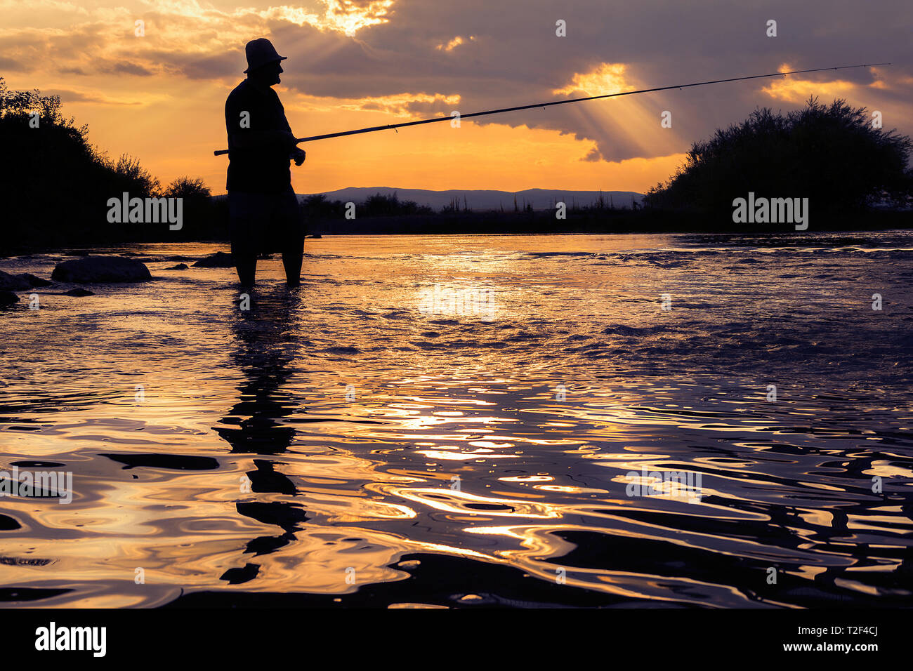 Fisherman silhouette standing in the water with his rod at sunset with ...