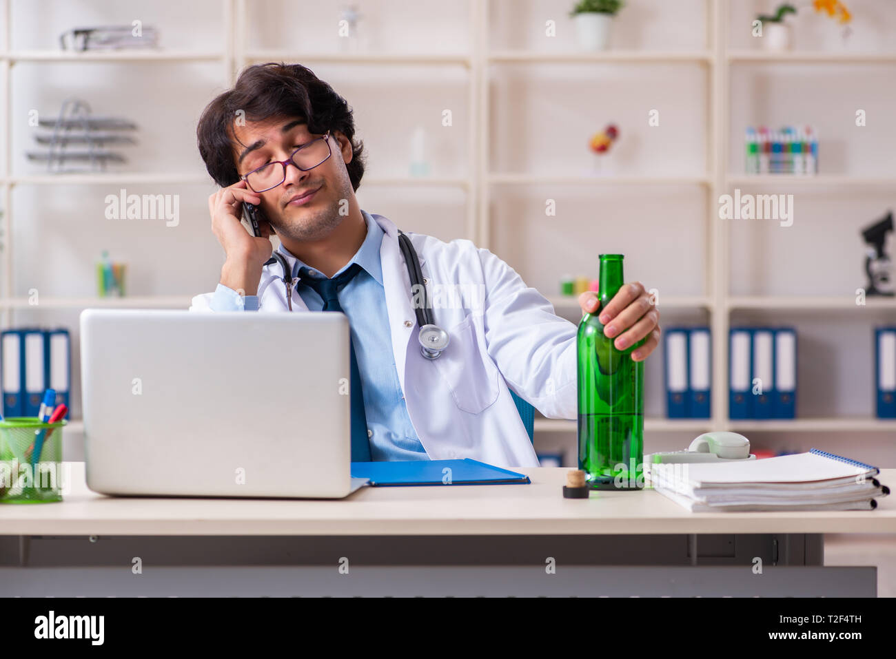 Young male doctor drinking in the office Stock Photo - Alamy