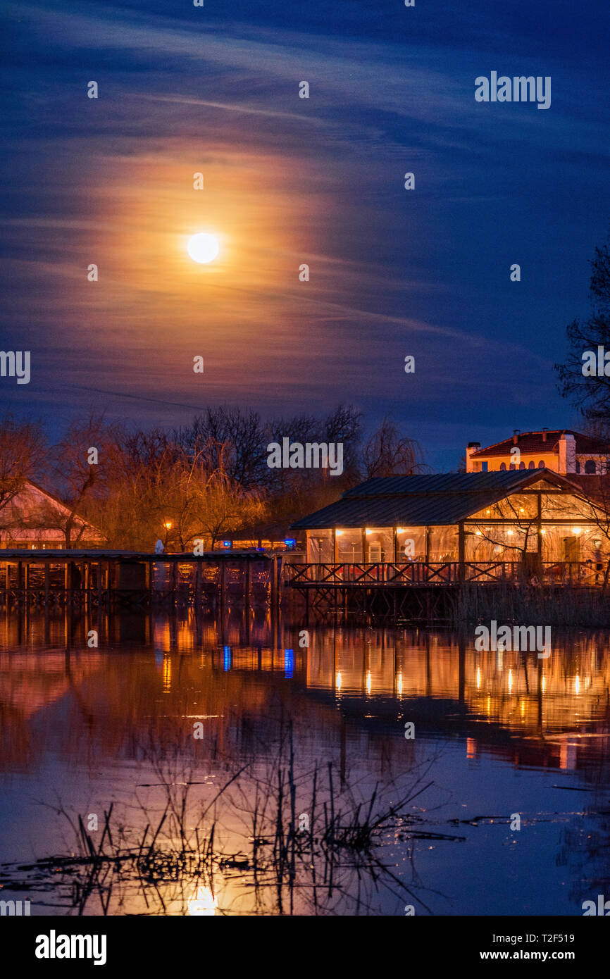 Beautiful night scene on the lake with a bright moon on the cloudy sky ...