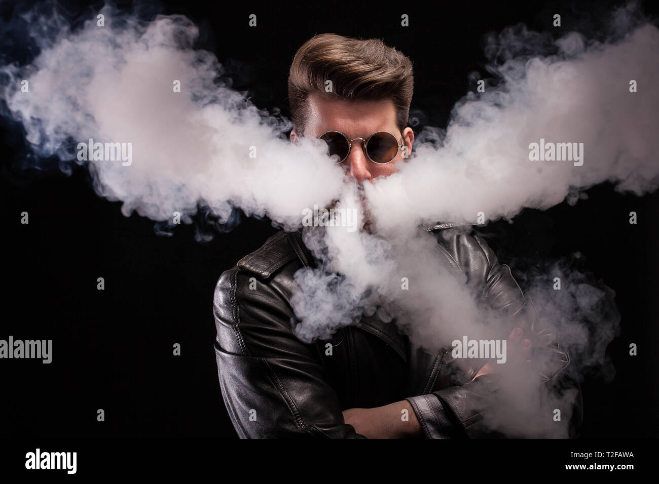 Fashionable bearded man with stylish glasses in leather jacket vaping ...