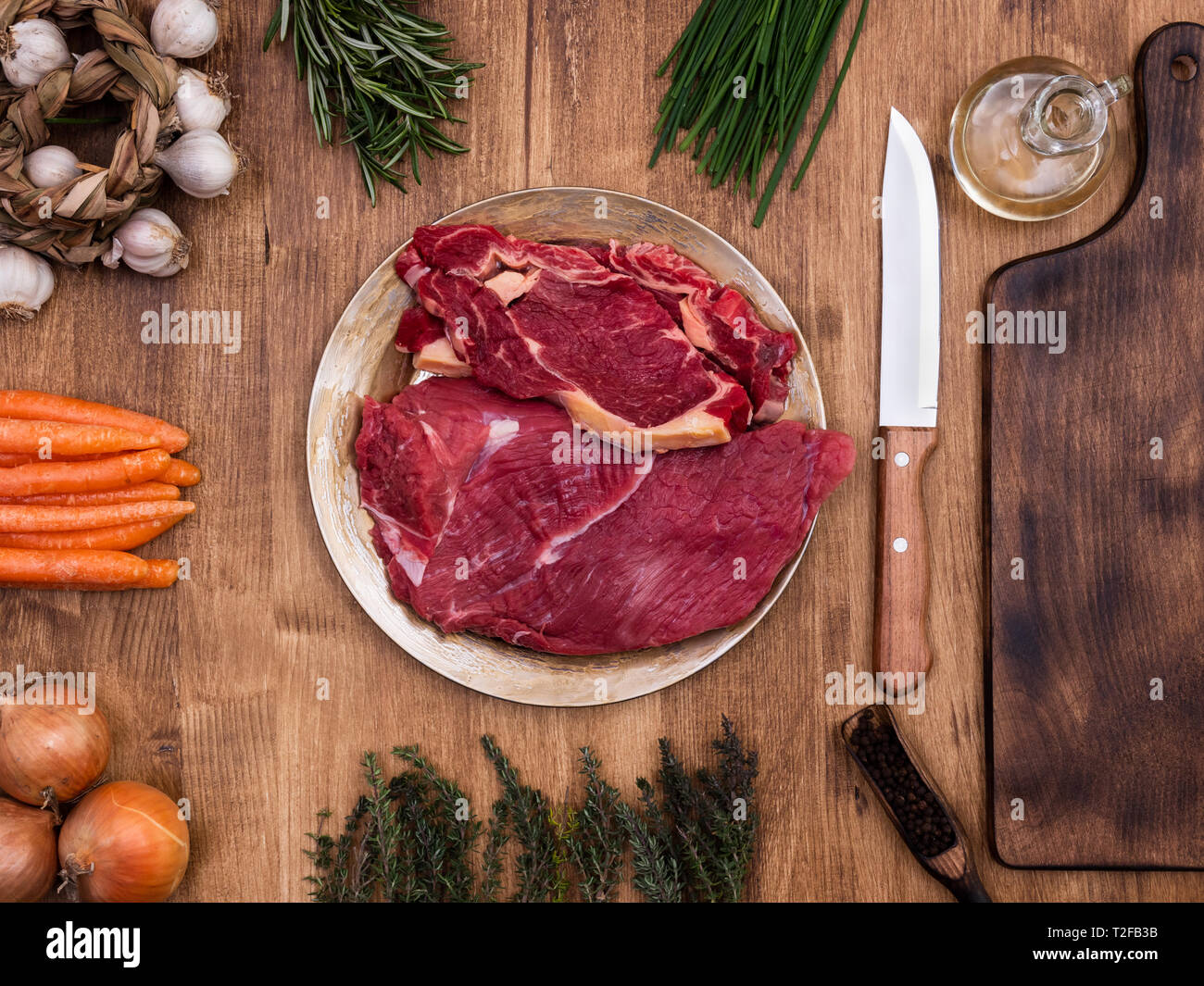 Fresh vegetables on wooden table with two chunks of red meat in centre ...