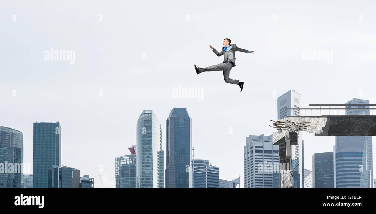 Businessman jumping over huge gap in concrete bridge as symbol of ...
