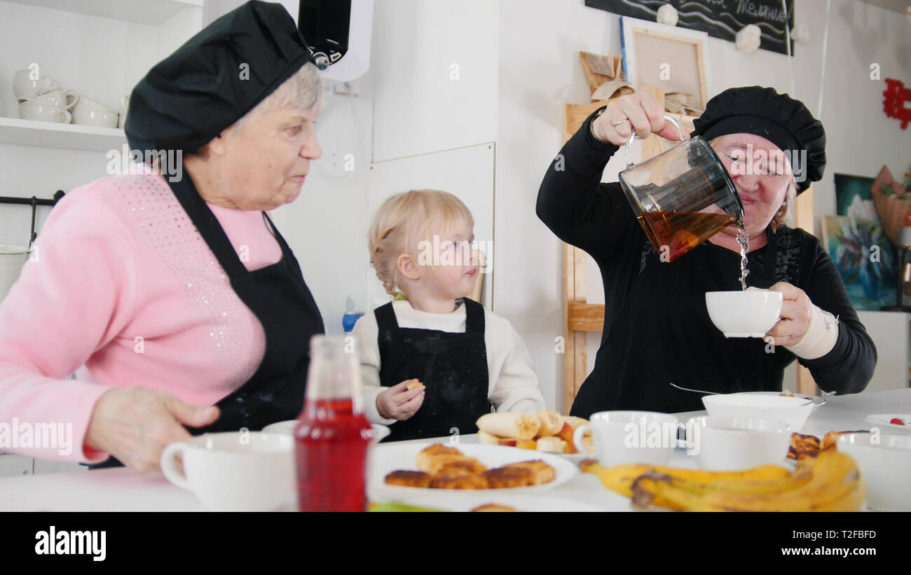 Family eating pancakes and drinking tea in the kitchen. Pouring the tea ...