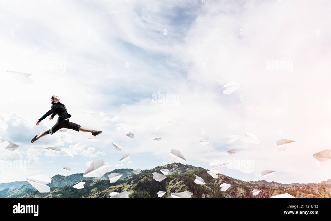 Attractive business woman in suit jumping in the air among flying paper ...