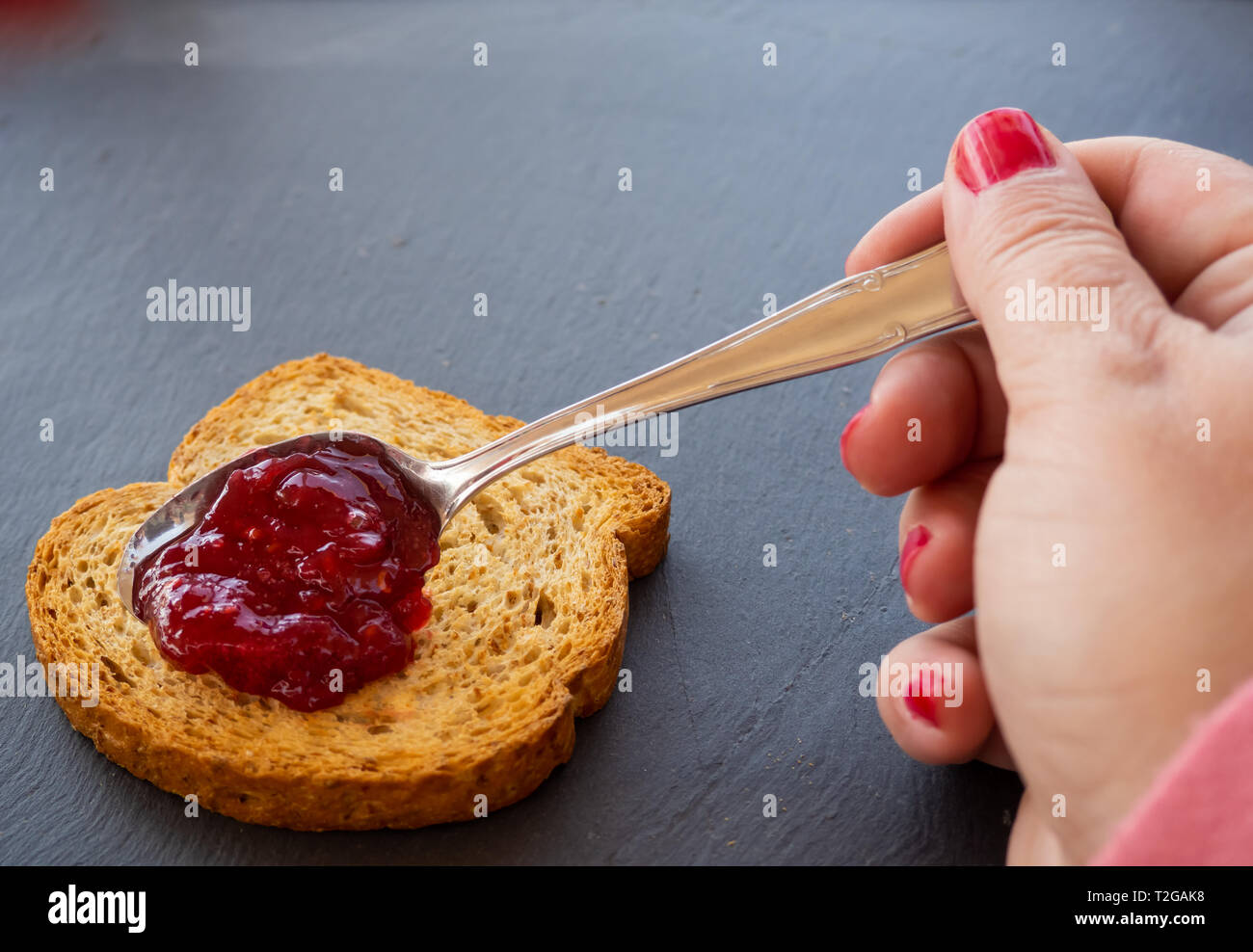 A woman with painted nails smearing red raspberry jam with a spoon on a ...