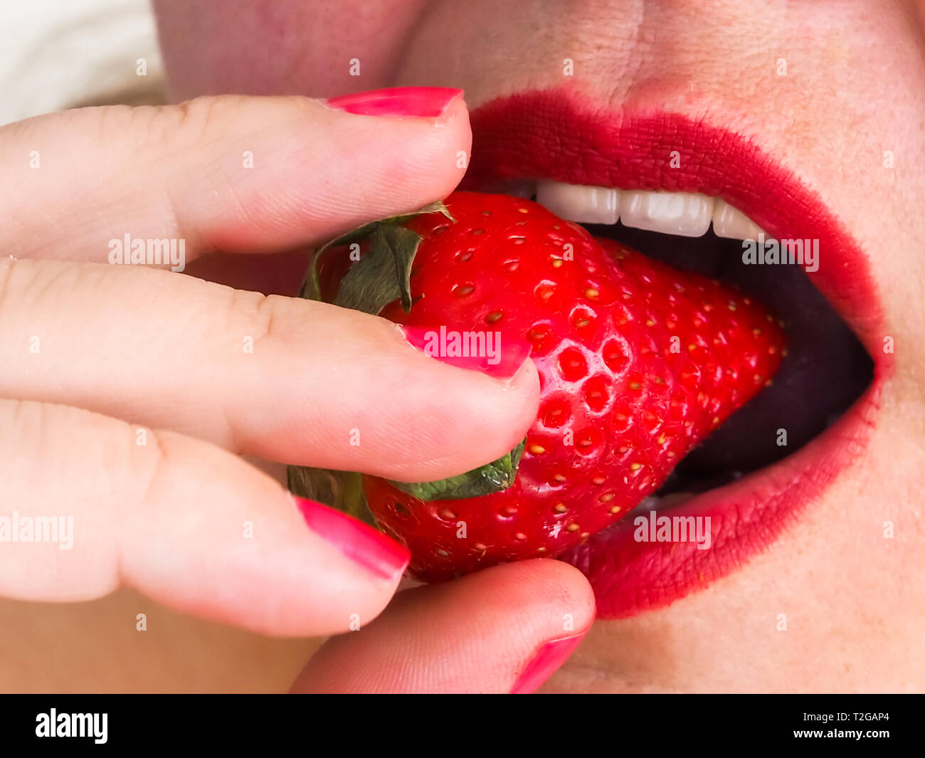 An adult woman with red nails and lips eating a strawberry Stock Photo ...