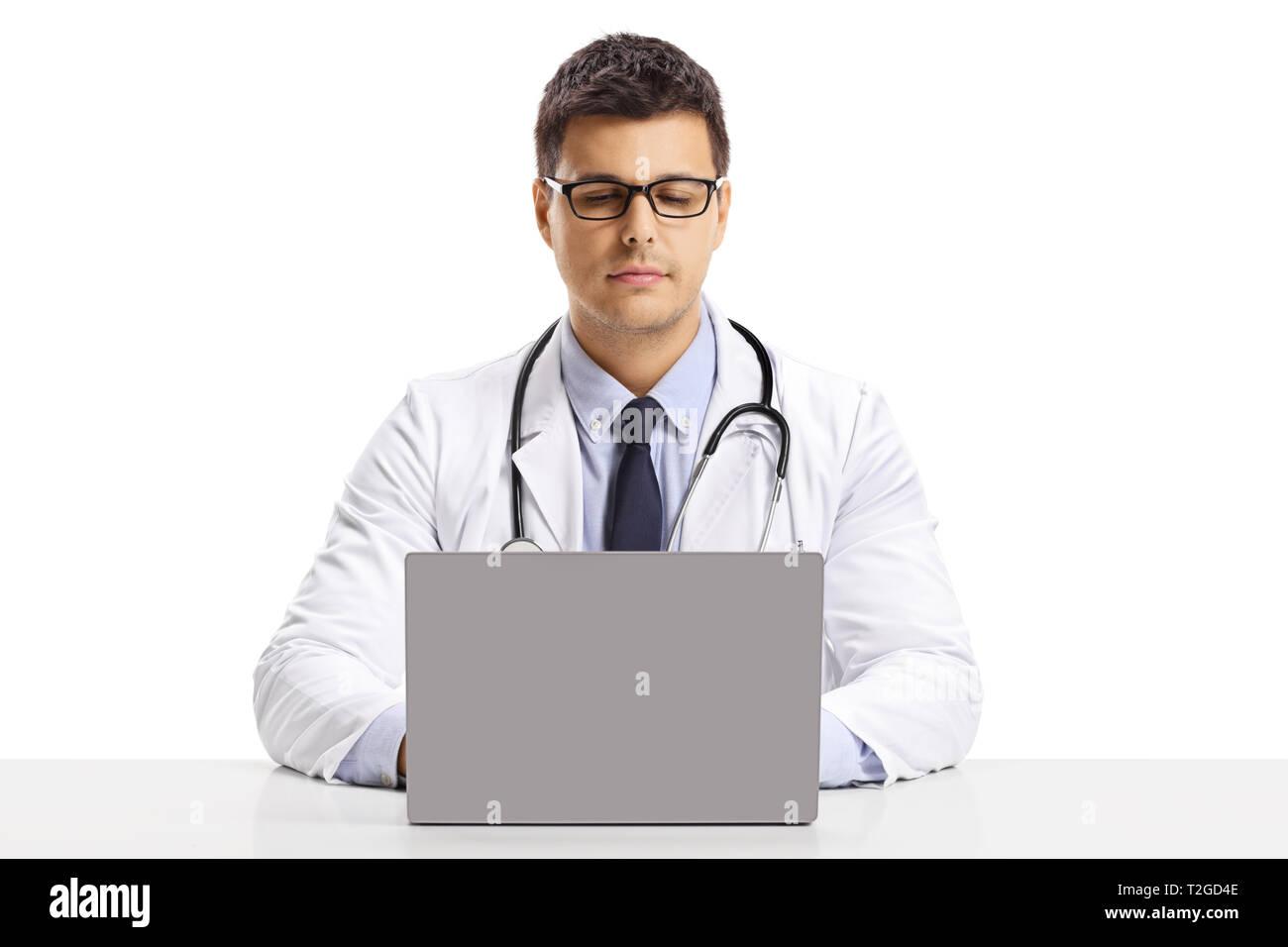 Young male doctor sitting at a desk and working on a laptop isolated on ...