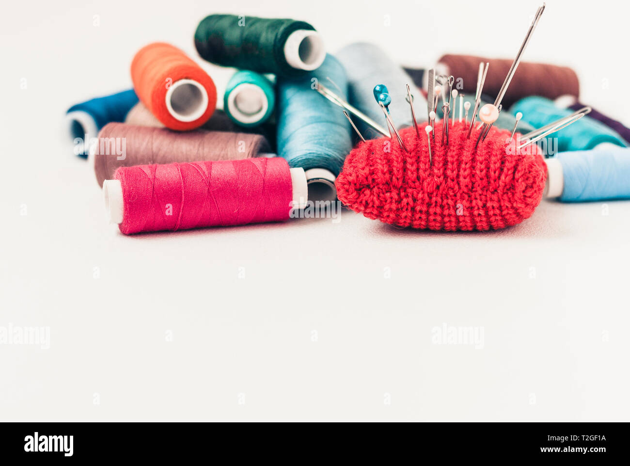 Red knitted needle pad for sewing and colored thread coils on white ...