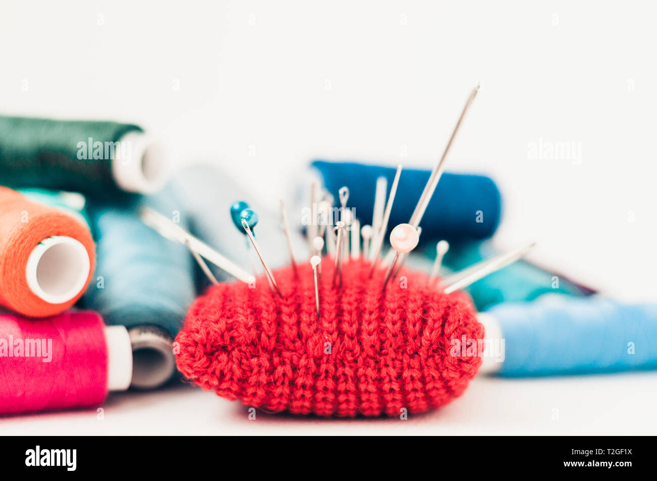 Red knitted needle pad for sewing and colored thread coils on white ...